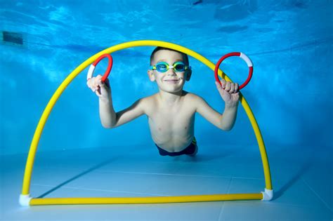 어린이 수영장에서 수중 수업에 있는 어린 소년의 초상화 그는 후프를 통해 수영 장난감을 꺼내 활동적인 행복한 아이 건강한 라이프 스타일 물 속에서 수영 레슨 가족 스포츠