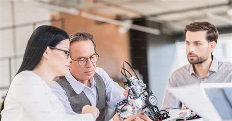 우리의 기술 프로젝트 세심한 집중 작업자는 테이블에 앉아 로봇을 들고 관심을 표명합니다 안경을 쓴 노인이 메커니즘을 골똘히