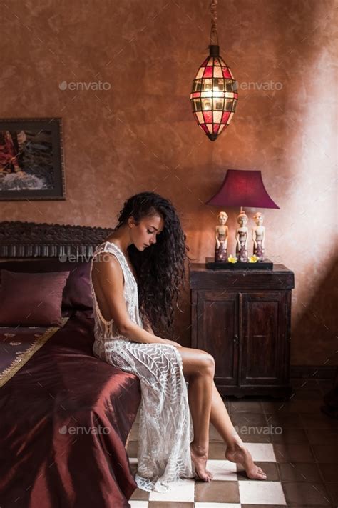 Woman With Long Black Hair In White Silk Lingerie Sitting On The Bed In