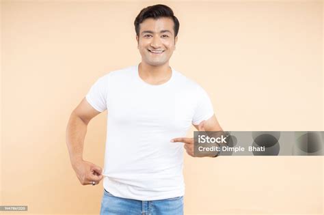하얀 캐주얼 티셔츠를 입은 잘생긴 젊은 인도 남자가 빈 공간을 손가락으로 가리키고 있다 모형 디자인 인쇄의 정면도입니다 Pointing At Self에 대한 스톡 사진 및