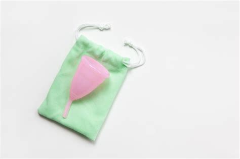 흰색 배경에 녹색 작은 가방에 분홍색 생리 컵 개념 제로 폐기물 저축 미니멀리즘 요즘 여성 위생 제품 플랫 레이 복사 공간 수평