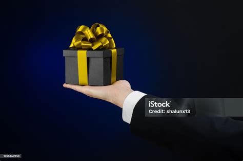 축 하와 선물의 테마 절연 스튜디오에 진한 파란색 배경에 골드 리본 아름 다운 블랙 박스에 포장 하는 독점적인 선물 비싼 선물을 들고 검은 양복에 남자 검은색에 대한 스톡