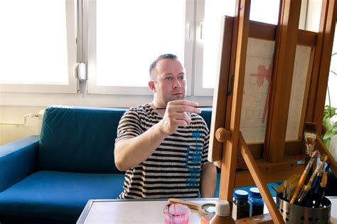 아트 페인트 스튜디오에서 나무 드로잉 보드 이젤에 캔버스와 워크샵에서 작업장에서 작업하는 남성 화가 페인트 브러시를 가진 예술가의 초상화는 오일 페인트로 캔버스에