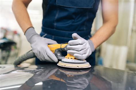 보호 장갑을 낀 알아볼 수 없는 정비사 남성이 자동차 수리 및 주유소 갱신 시 연삭 장치를 사용하여 검은색 후드를 닦는 모습의 자른 사진 25 29세에 대한 스톡 사진 및