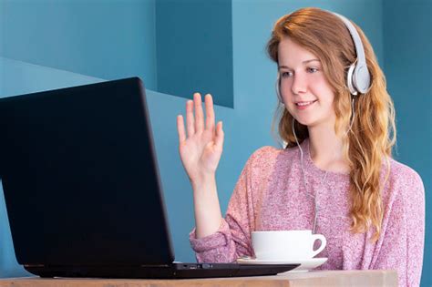 헤드폰을 착용 한 소녀가 노트북에서 화상 채팅을 통해 통신합니다 원격 작업 온라인 커피 한 잔과 함께 카페에있는 소녀 손을 흔들고 인사 공부에 대한 스톡 사진 및 기타