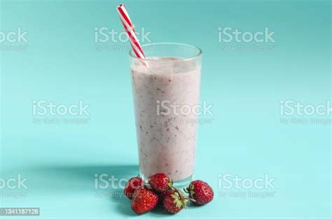 투명한 유리에 딸기와 빨간 빨대가 있는 밀크쉐이크가 파란색 배경을 클로즈업합니다 색을 입은 배경에 아이스크림 우유 열매의 칵테일