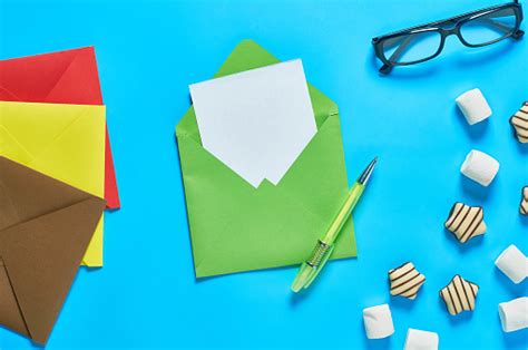 흩어져있는 줄무늬 사탕 빈 종이 시트 안경 펜이있는 녹색 봉투 근처의 마시멜로가 파란색 책상위에 놓여 있습니다 러브 레터 컨셉 맨 위 보기 클로즈업 갈색에 대한 스톡 사진