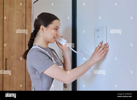 Teenage Girl Holding Intercom Handset While Talking To Guest Stock