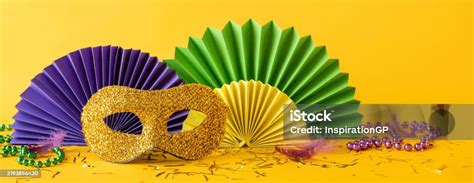 마디 그라 축하 테마를 묘사 한 밝은 노란색 배경에 녹색과 보라색 부채와 구슬로 배열 된 반짝이는 질감의 황금 마스크의 측면보기 사진 Mardi Gras에 대한 스톡 사진