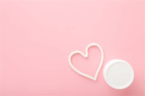크림으로 만든 하트 모양 밝은 분홍색 테이블 배경에 흰색 항아리 파스텔 색상 얼굴 손 다리 바디 스킨에 신경을 쓰다 근접 촬영 텍스트 또는 로고의 빈 장소입니다 하향 보기