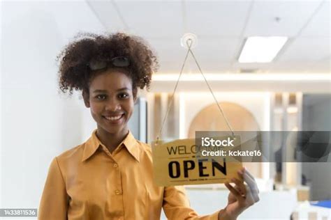 여성 상점 주인은 문 유리를 통해 열린 표지판을 넓게 돌리고 서비스 할 준비가되었습니다 재개 표지판을 돌리는 중소기업 여성 주인