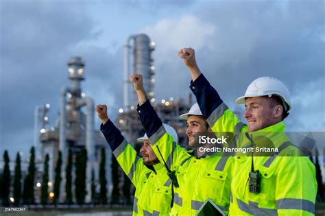 공장 엔지니어 또는 기술자 근로자는 줄에 서서 오른손을 들고 왼쪽을 보고 저녁 햇살 동안 정유 및 석유 화학 공장 앞에 서 있습니다 25 29세에 대한 스톡 사진 및 기타