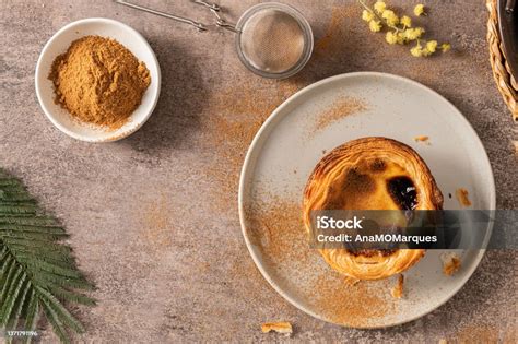 전통적인 포르투갈 페이스트리 파스텔 데 나타 또는 파스텔 드 벨렘은 소박한 보드에 전통적인 트레이에 계피 파우더를 드실 수 있습니다 달걀 타르트 벨렘 리스본에 대한 스톡