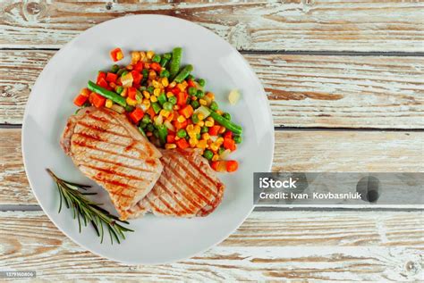 구운 고기 조각 로즈마리와 후추를 화이트 플레이트에 곁들인 스테이크 스테이크 근처의 옥수수 당근 녹색 완두콩 샐러드 플레이트