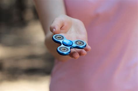 회색 배경 스트레스와 이완 Fidgets 안티 불안 구제 장난감 인기 있는 피 젯 회전자 장난감을 들고 거리 여성 손에 손에 파란 금속 회전자를 재생 하는 여자 강철에 대한