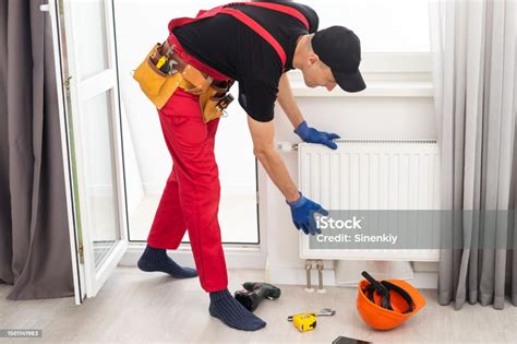 방에 난방 라디에이터를 설치하는 동안 렌치를 사용하여 작업 바지에 남자 젊은 배관공 아파트에 난방 시스템을 설치 라디에이터 설치 배관 작업 및 주택 개조의 개념 가정의 방에