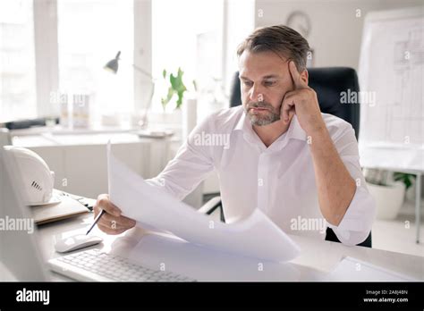 Mature Pensive Engineer Looking At Sketch While Thinking Of Ideas Or