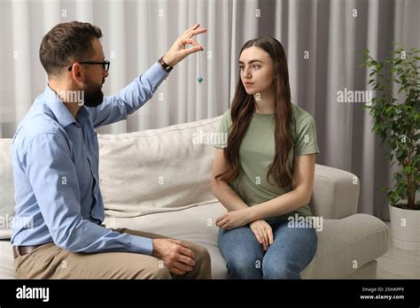 Psychologist using pendulum while working with patient during hypnosis session indoors Stock ...