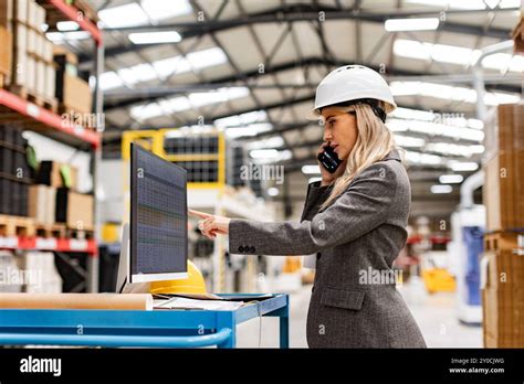 Female Engineer Project Manager Standing In Modern Industrial Factory By Computer Making Phone