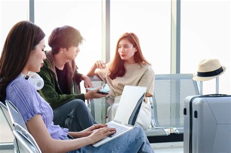 아시아 소녀 여행자는 수하물 가방을 들고 터미널 의자에 앉아 노트북 계산작업을 하고 공항에서 배경에서 이야기하는 다른 승객들 휴가 중인 관광 대기 항공사 항공편 여행 20