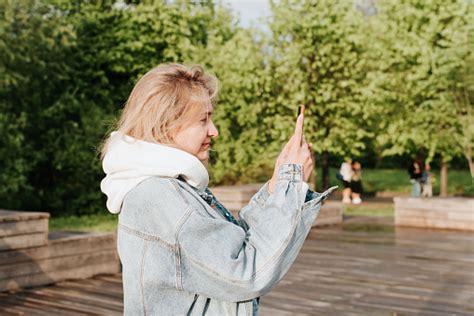 아름다운 젊은 여성은 야외에서 휴대 전화 카메라에서 뭔가를 촬영합니다 여름 화창한 날에 스마트 폰을 사용하여 청바지에 미소 힙스터 소녀 프로필 생활방식 35 39세에 대한