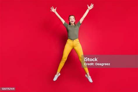 미친 밀레니얼 아가씨 점프 높은 지출 자유 시간 흥분 쾌활한 분위기 착용 캐주얼 옐로우 바지 녹색 티셔츠 고립 된 붉은 색 배경의 전체 길이 사진 십대에 대한 스톡 사진 및