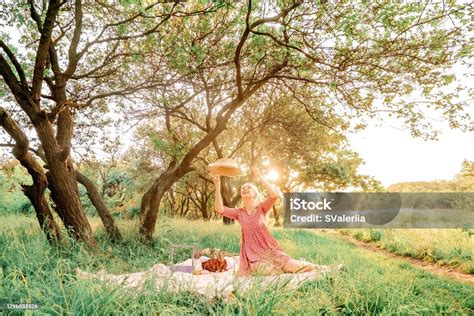 봄 공원에서 피크닉에 분홍색 드레스와 밀짚 모자를 입은 아름다운 소녀 한 여성이 큰 가지 나무 밑에 혼자 앉아 있다 봄에 대한 스톡 사진 및 기타 이미지 Istock