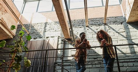 세련된 캐주얼 웨어를 입은 젊은 인종 데이트 로프트 아파트나 스튜디오의 발코니에 서서 회색 벽돌 벽을 들고 대화를 나눴다 사진