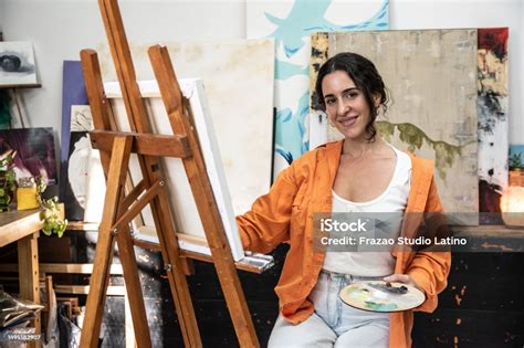 집에서 예술가의 팔레트를 들고 있는 동안 캔버스에 그림을 그리는 중년 여성의 초상화 화가 예술가에 대한 스톡 사진 및 기타