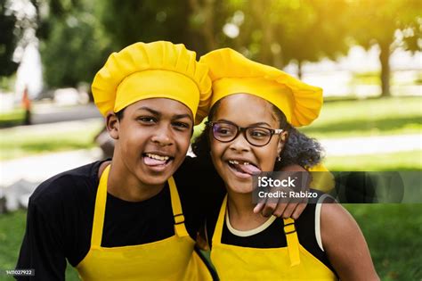 아프리카 어린이들은 요리사 모자와 노란 유니폼을 입고 서로 혀를 내밀며 요리합니다 아프리카 십대와 흑인 소녀는 재미 있고 음식을