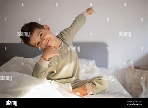 Cheerful Energy Cute Little Boy Sits On Bed Woke Up And Raises His