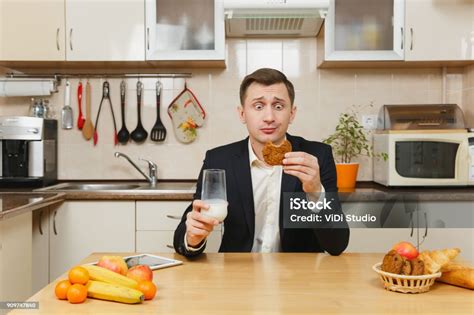 잘생긴 백인 젊은 비즈니스 남자가 양복 셔츠 가벼운 부엌에 우유와 귀리 쿠키를 먹는 데 아침 식사 테이블에 앉아 있다 다이어트 개념입니다 건강 한 생활양식입니다 요리 음식