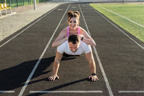 Loving Couple Trains Together At The Stadium A Man Does Push Ups And A