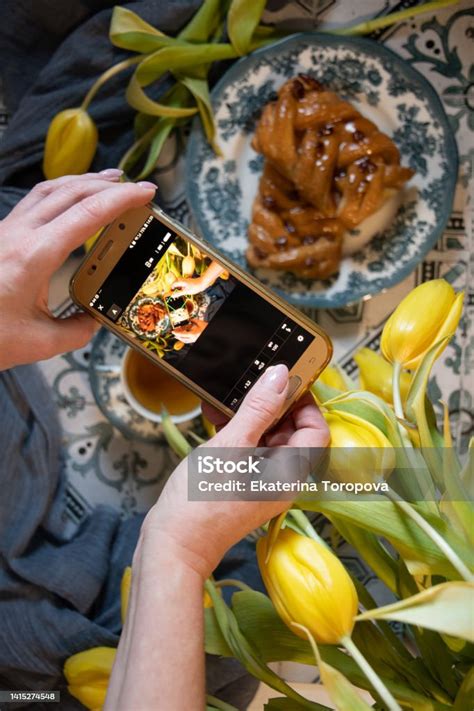 여성 음식 블로거는 노란색 튤립 차 한 잔 휴대 전화의 케이크로 아름답게 설정된 테이블 사진을 찍습니다 귀여운에 대한 스톡 사진