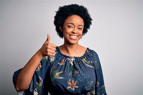 젊은 아름 다운 아프리카 계 미국인 Afro 여자 곱슬 머리 캐주얼 꽃 드레스를 입고 행복 한 엄지 손가락 을 하 고 손으로 제스처 성공을 보여주는 카메라를 보고 표정을