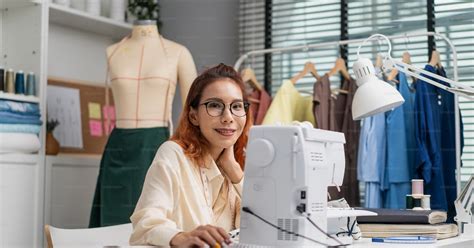 아시아의 젊은 재단사 소녀는 아틀리에를 재단하고 카메라를 봅니다 매력적인 젊은 여성 패션 디자이너는 작업장에서 새로운 수제