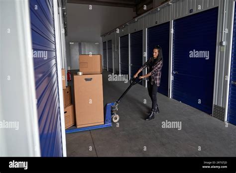 Full Body Side View Of Female Rolling Pallet Jack With Heap Of Carton Boxes Into Self Storage