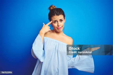 파란색 고립 된 배경에 롤빵 헤어 스타일을 입고 젊은 아름다운 여성은 혼란과 이마에 손가락을 가리키는 복사 공간을 보여주는 열린 손바닥짜증 그것에 대해서 생각해 봐