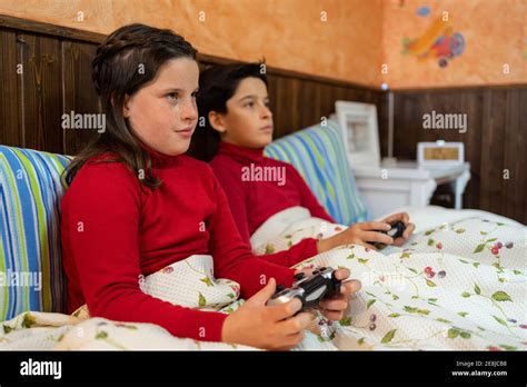 Cheerful Teenage Brother And Sister Sitting On Bed And Playing