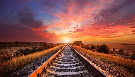 Vibrant Sunset Over A Railway Track Stretching Towards The Horizon