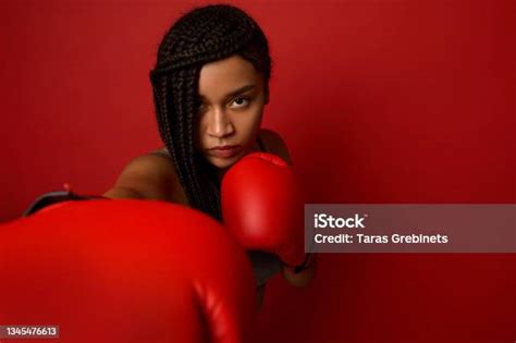빨간 권투 장갑을 쓰고 직접 히트 복사 공간으로 빨간색 배경에 고립 된 집중 젊은 아프리카 스포츠 여자 복서의 클로즈업 초상화 블랙 여자 복서 펀칭 향해 카메라 무에타이에