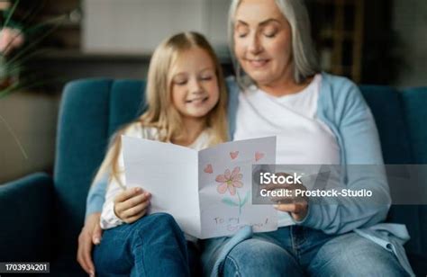쾌활한 백인 작은 손녀와 성숙한 할머니가 그림 엽서를 주고 소파에서 책을 읽는다 읽기에 대한 스톡 사진 및 기타 이미지 읽기 아이 주기 Istock