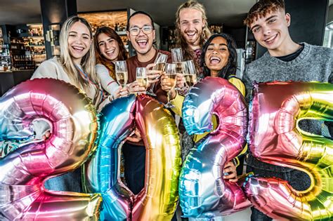 샴페인 와인을 응원하고 바 레스토랑에서 새로운 2025 년을 축하하는 행복한 친구들 겨울 방학에 집에서 새해 파티를 만드는 손에 풍선을 들고 웃는 젊은 Multietnic