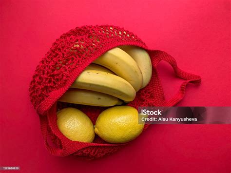 과일이 있는 스트링 백 빨간 배경에 빨간 문자열 가방에 바나나와 레몬 위에서 사진 과일이 있는 니트 백 폐기물이 없습니다 과일은 노란색입니다 0명에 대한 스톡 사진 및 기타