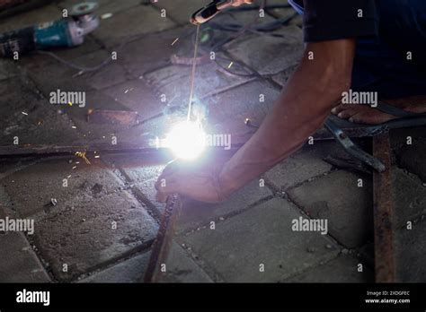 A Person Welding Metal Pieces Together On A Tiled Floor With Sparks Flying Stock Photo Alamy