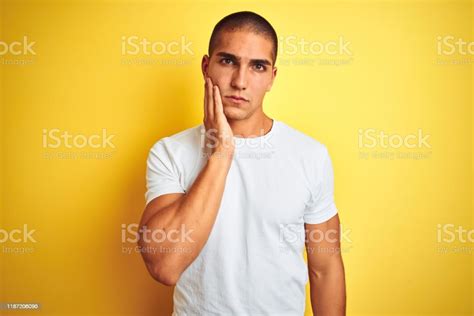 노란 고립 된 배경 위에 캐주얼 한 흰색 티셔츠를 입은 젊은 백인 남성은 치아에 치통이나 치과 질환으로 인해 고통스러운 표정으로