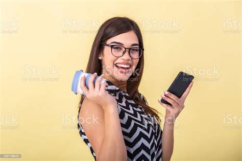 한 손에는 커피 한 잔을 다른 한 손에는 스마트폰을 가지고 있는 여성 갈색 머리 소녀 와 어두운 머리 마시는 커피 와 서핑 그물 행복한 여자 표정 긍정적인 감정 표현에 대한