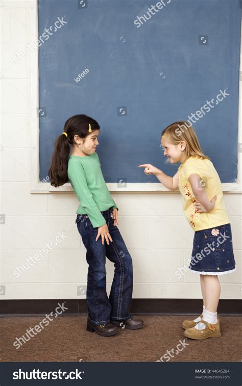 girl pointing finger at other girl in school classroom vertically