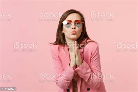 심장 안경에 기도 젊은 여자의 초상화 스튜디오에서 파스텔 분홍색 벽 배경에 고립 된 손을 잡고 입술을 불고 사람들은 진심으로 감정 라이프 스타일 개념입니다 복사 공간을 모의