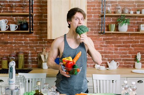 건강하고 비건 식품 컨셉 부엌에서 신선한 야채와 그릇을 들고있는 동안 브로콜리를 먹는 회색 셔츠에 잘 생긴 재미 남자 가정 생활에 대한 스톡 사진 및 기타 이미지 Istock